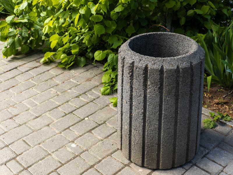 A Large Stone Trash Can Sitting on a Brick Walkway Next To a Bush Stock ...