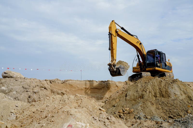 A Large Yellow Backhoe is Planting and Grading Brown Rays in a Factory ...