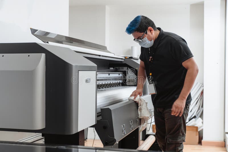 Latin American Worker with a Mask Cleaning a Large Format Plotter in ...