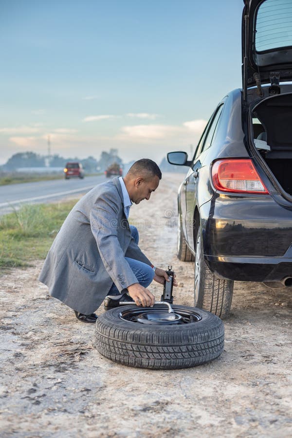 Latino Man Changes a Flat Tire on His Car at the Side of the Road Stock ...