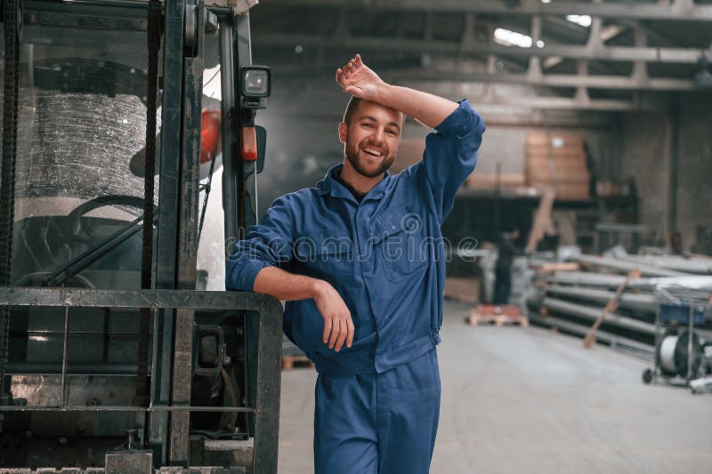 Leaning on the Forklift. Factory Worker in Blue Uniform is Indoors ...