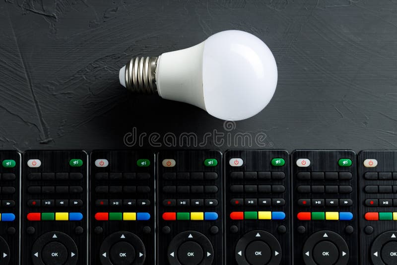 The LED Light Bulb on a Dark Background and the TV Remotes Under it ...