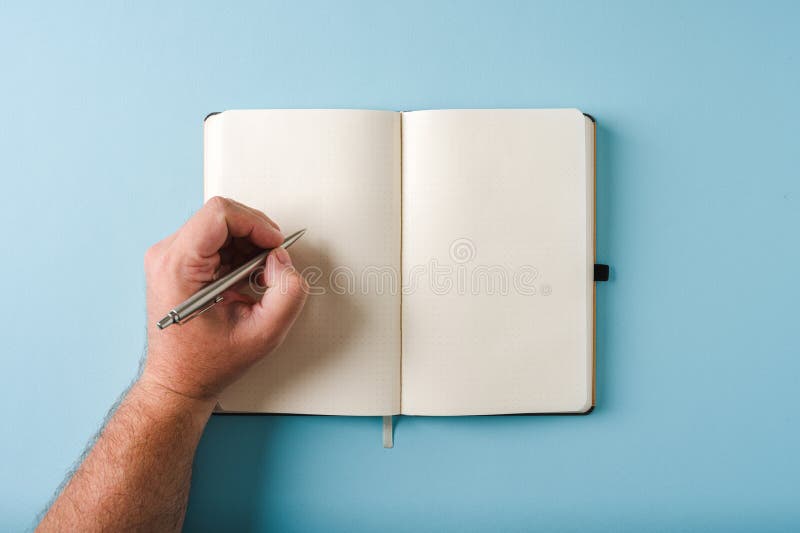 Left Hand Holding a Ballpoint Pen on an Open Notebook on a Blue ...