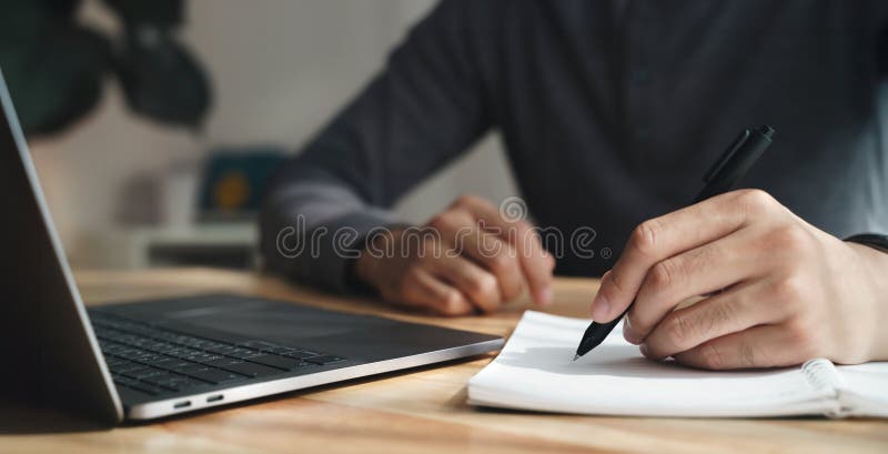 Left Handed Man Writes in a Notebook on the Table with Laptop Computer ...