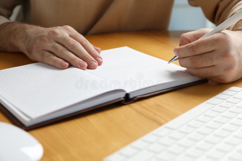 Left-handed Man Writing in Notebook at Wooden Desk, Closeup Stock Photo ...