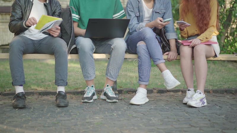 Legs of Four Caucasian University Students Sitting on Bench Outdoors ...