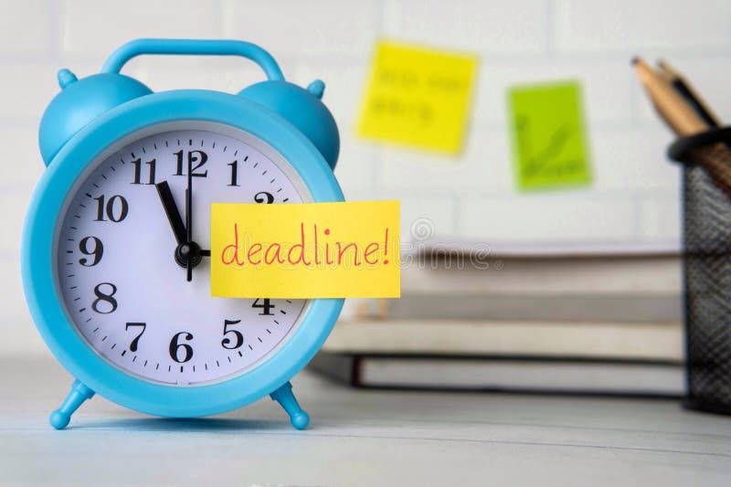 A Light Blue Alarm Clock and a Sticky Note with Blurred Stacks of Books ...