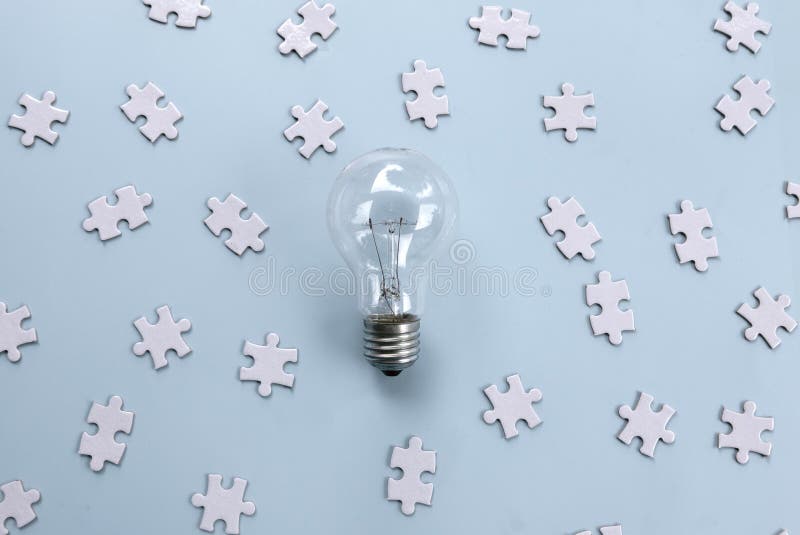 Light Bulb Centered on Scattered Jigsaw Puzzle Pieces Against a Blue ...