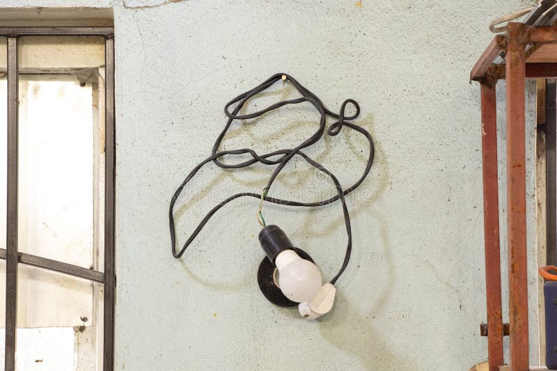 A Light Bulb in a Socket and a Black Cable Hanging on the Wall Near a ...