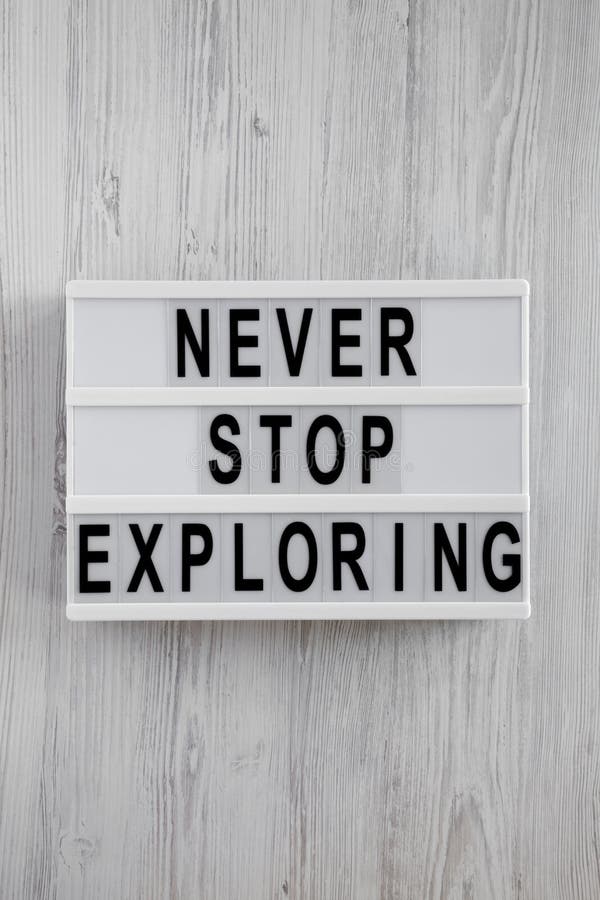 Lightbox with Text `Never Stop Exploring` Over White Wooden Surface ...