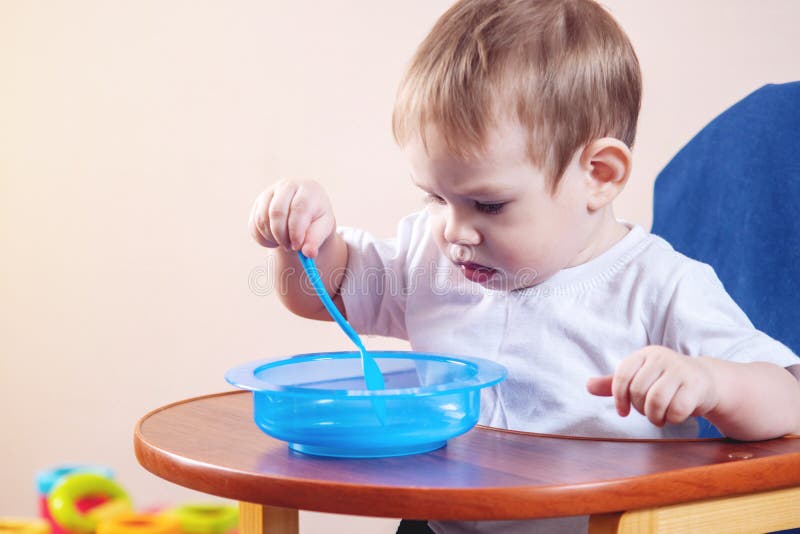 Little Baby Boy Learning To Eat at the Kid Table Studying a Plate and ...
