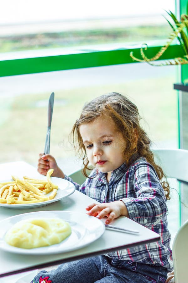 Little Baby Girl Sitting in the Restaurant or Cafe and Eating Food ... Little Baby Girl Sitting in the Restaurant or Cafe and Eating Food ...