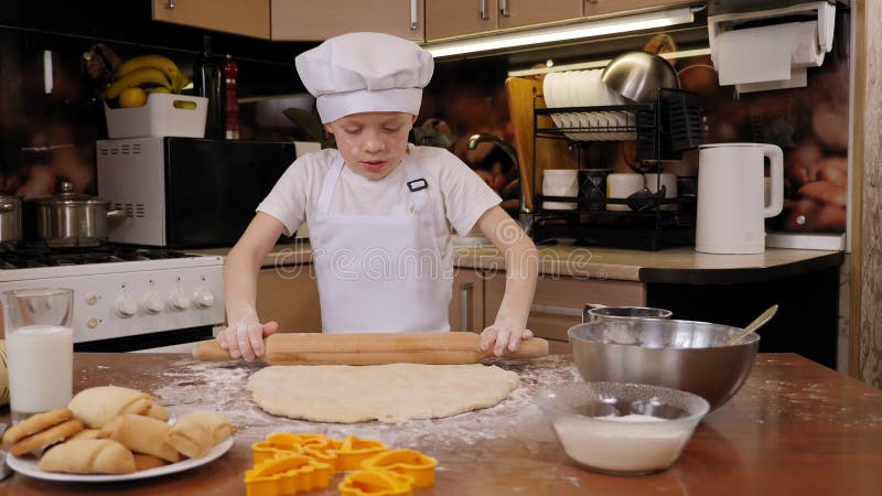 A Little Boy in an Apron Rolls Out the Dough Using a Rolling Pin in the ...