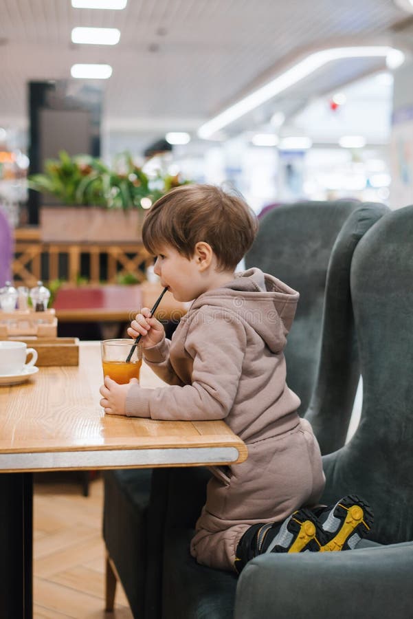 Little Boy Child Drinks Juice from a Straw while Sitting at a Table in ...