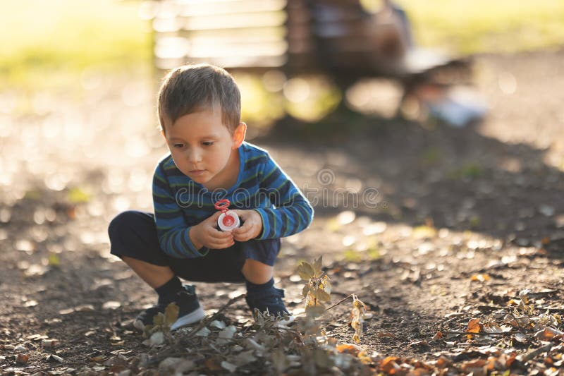 Little Boy Crouched in the Park Holding Soap Bubbles Stick Stock Photo ...