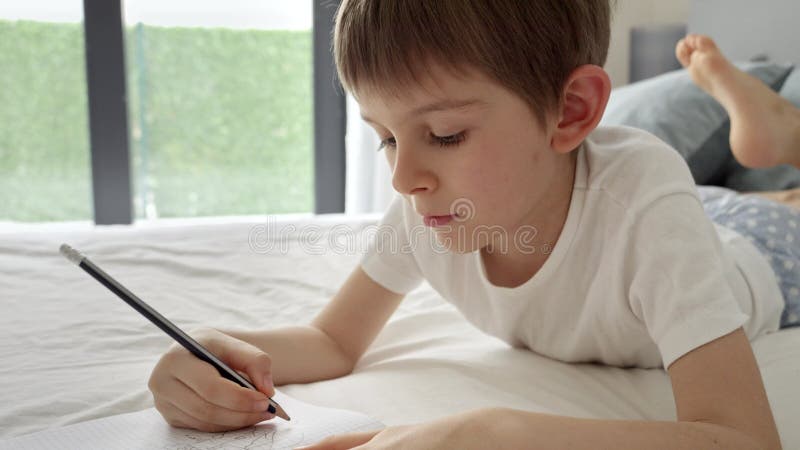Little Boy Doing His Homework in Bed, Writing in a Notebook with ...