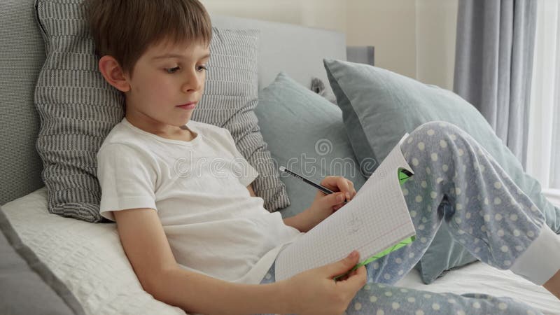 Little Boy is Doing Homework in Bed, Writing in a Notebook. Concept of ...