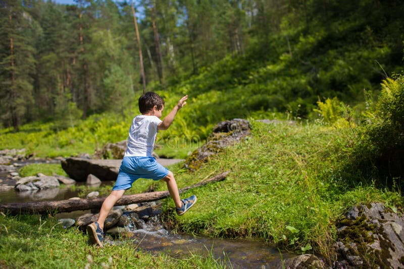 Little Boy Jumps Over a Stream in Forest Stock Image - Image of ...
