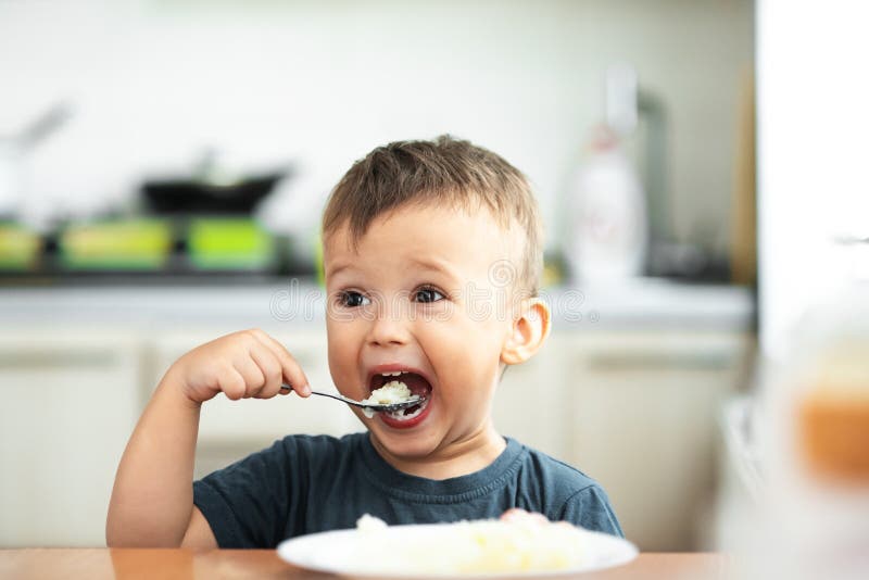 A Little Boy in the Kitchen Greedily Eats Rice with a Spoon Stock Image ...