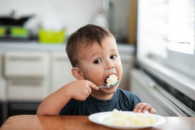A Little Boy in the Kitchen Greedily Eats Rice with a Spoon Stock Photo ...