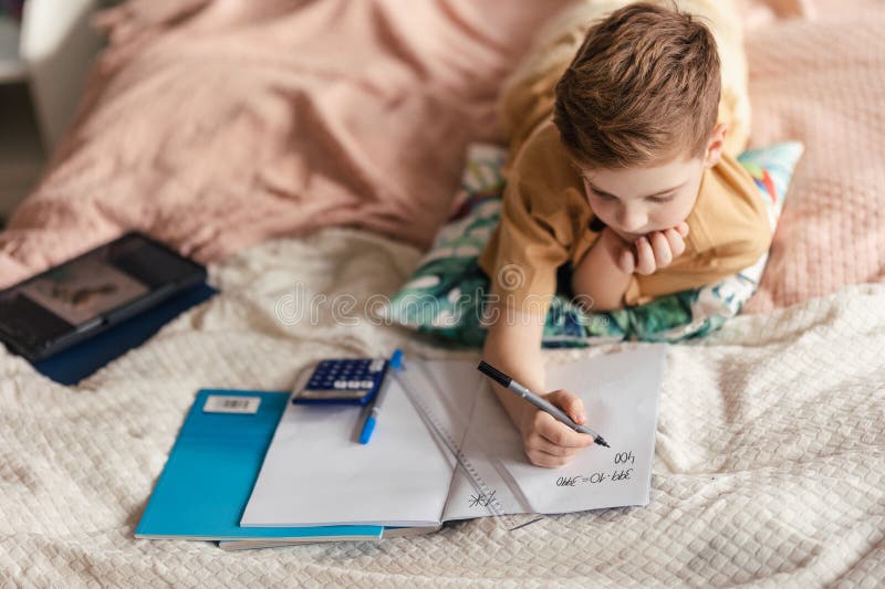 Little Boy Lying on a Bed and Doing His Homework. Stock Photo - Image ...