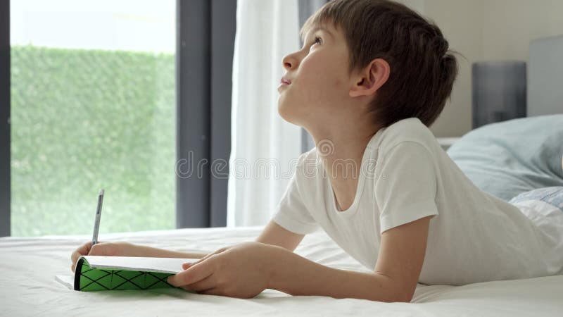 Little Boy Lying in Bed, Doing His Homework and Biting Pencil while ...