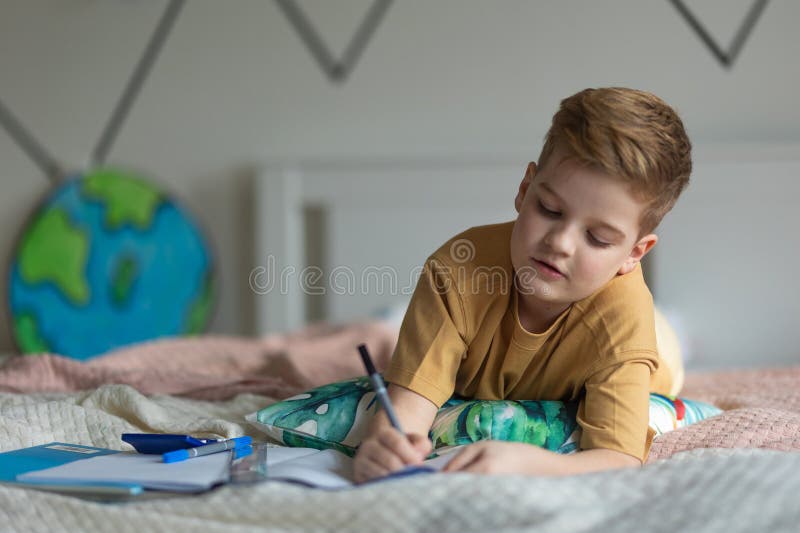 Little Boy Lying on a Bed and Doing His Homework. Stock Photo - Image ...