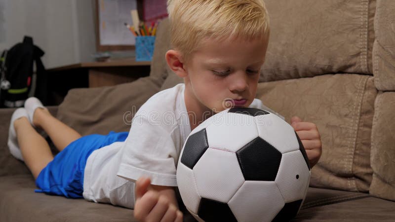 A Little Boy is Lying on the Couch at Home and Hugging a Soccer Ball ...