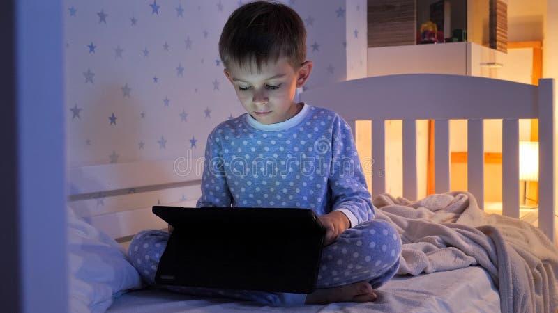 Little Boy in Pajamas Sitting on Bed at Night and Using Tablet Computer ...