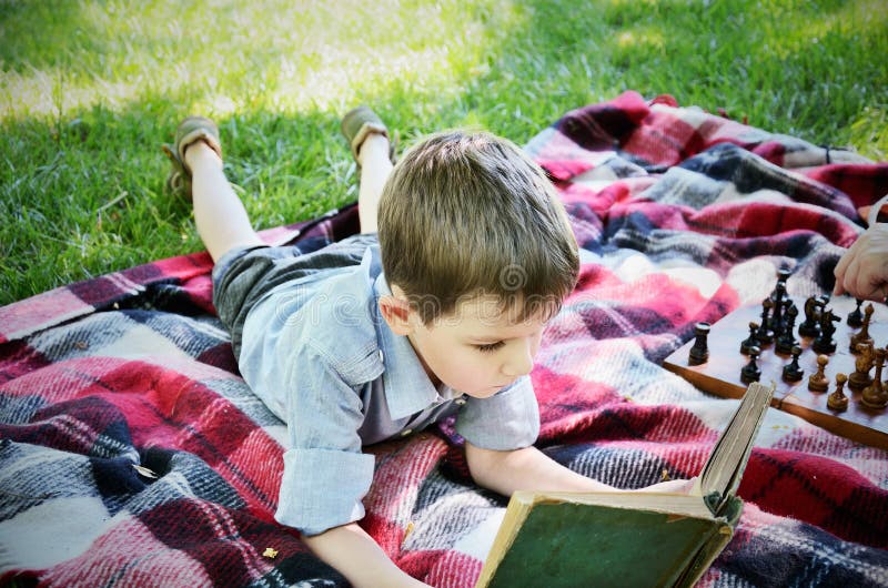 Little Boy Reading a Book while Lying on a Mat in the Park Stock Image ...
