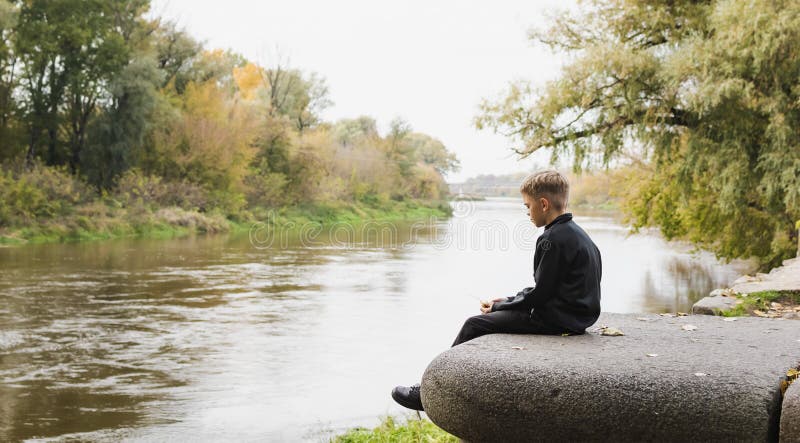A Little Boy is Sitting on the Bank of the River Stock Photo - Image of ...