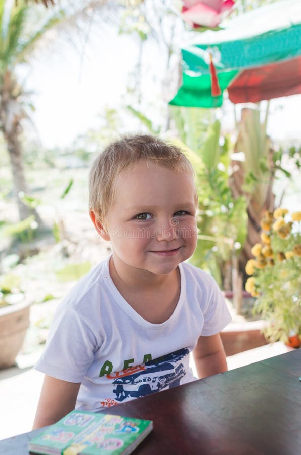 Little Boy is Sitting at a Table Next To a Book and Smiling Editorial ...