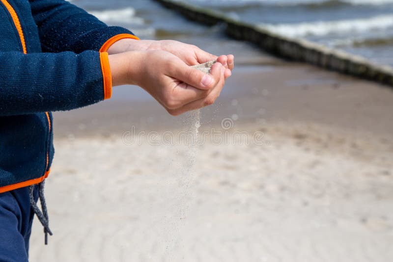 A Little Boy Slowly Lets Sand Flow through His Hands Scattered by the ...