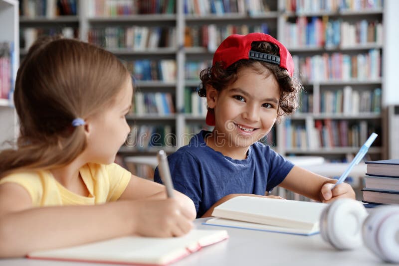 Little Children Writing at Table with Books in Library Stock Photo ...