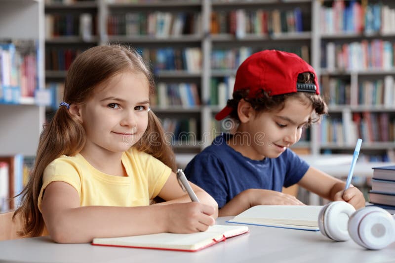 Little Children Writing at Table with Books in Library Stock Image ...