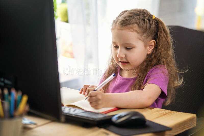 A Little Cute Girl Using Computer for Remote E-learning, , Writes in a ...