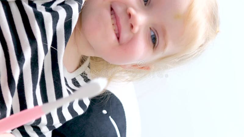 Little Girl in Hands with Toothbrush Smiles Bit Lip and Waves Head ... Little Girl in Hands with Toothbrush Smiles Bit Lip and Waves Head ...