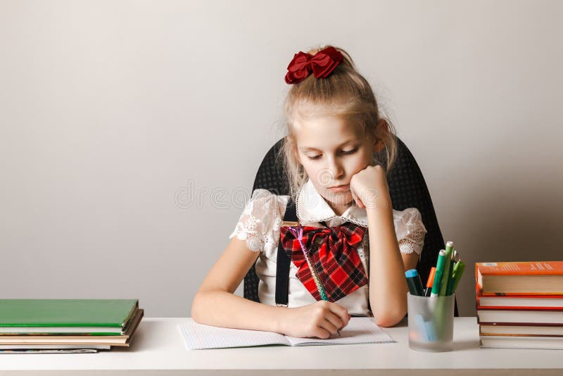 A Little Girl in a School Uniform is Doing Homework in a Exercise Book ...