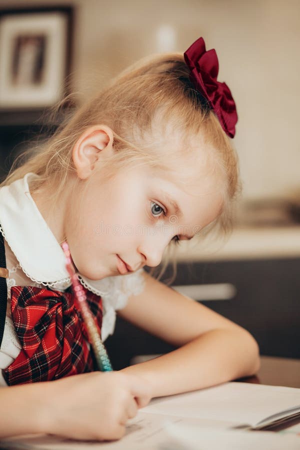 A Little Girl in a School Uniform is Doing Homework in a Exercise Book ...