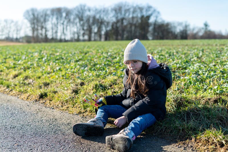 Little Girl Sitting on the Road in the Field and Playing with Grass ...