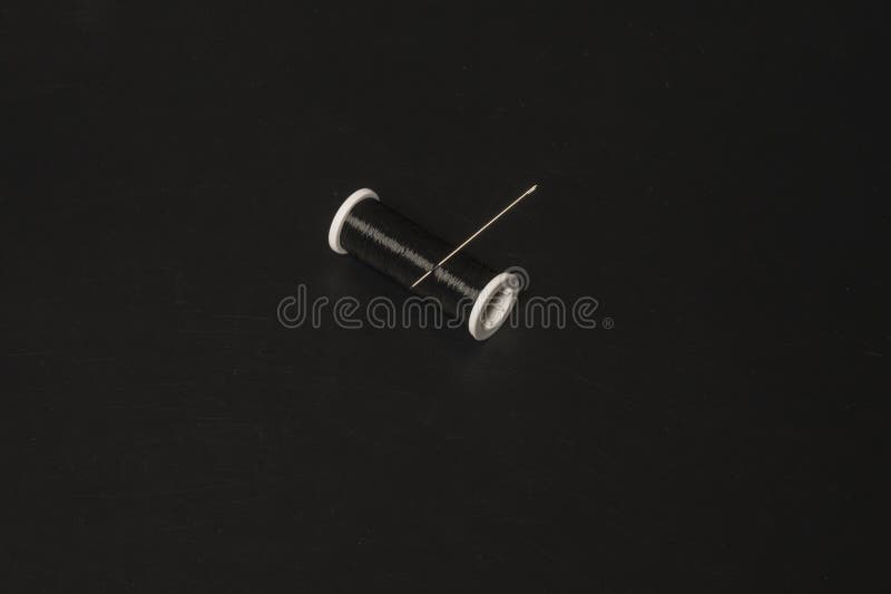 A Lone Spool of Shiny Black Thread with a Pricked Sewing Needle Lying ...