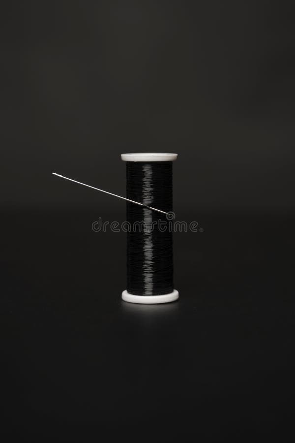 A Lone Spool of Shiny Black Thread with a Pricked Sewing Needle on a ...