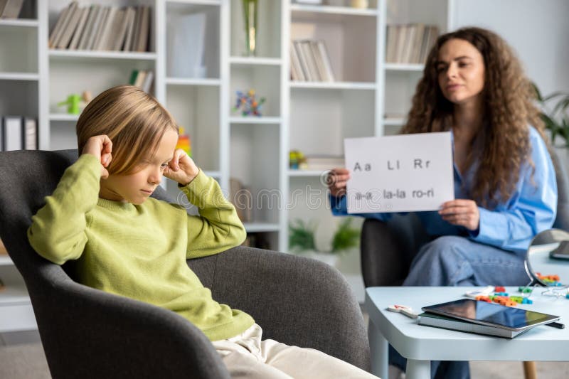 Long-haired Young Speech Therapist Working with a Blonde Boy and Both ...