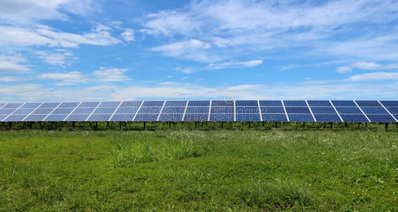 Long Row of Solar Panels in a Meadow, between Green Grass and Clouds ...