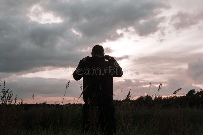 Lookig at the Back of a Man Standing in a Field. Holding His Hood ...