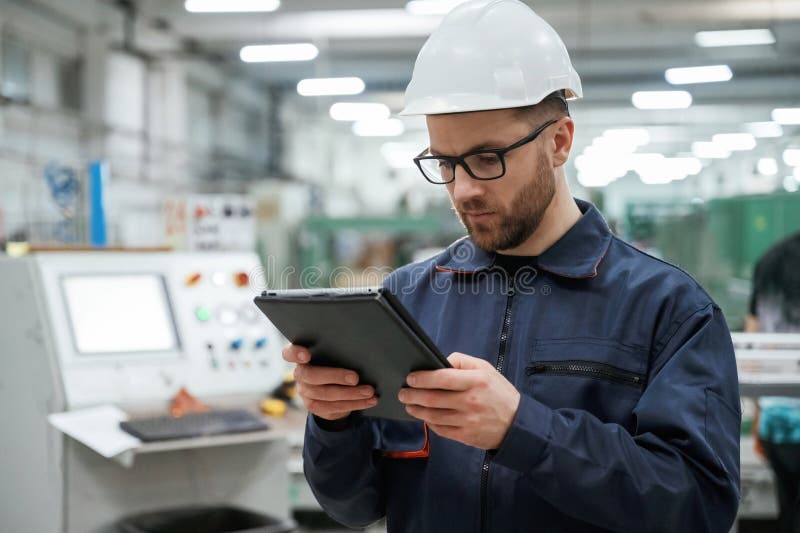 Looking and Holding Tablet. Factory Worker is Indoors with Hard Hat ...