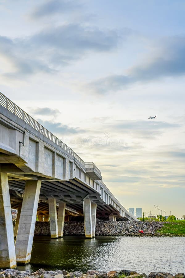 Viewing Concrete Bridge Over Water with Plane Flying in Cloudy Sky ...