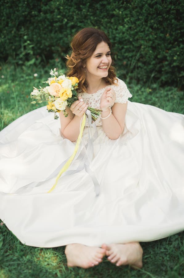 Lovely Bride Sitting on Ground Holding a Bouquet Smiling at Camera ...