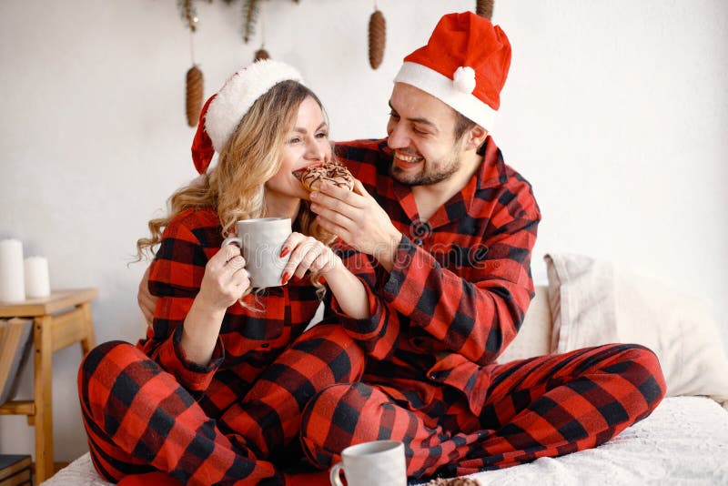 Couple Wearing Christmas Plaid Red Pajamas Sitting On The Bed Stock