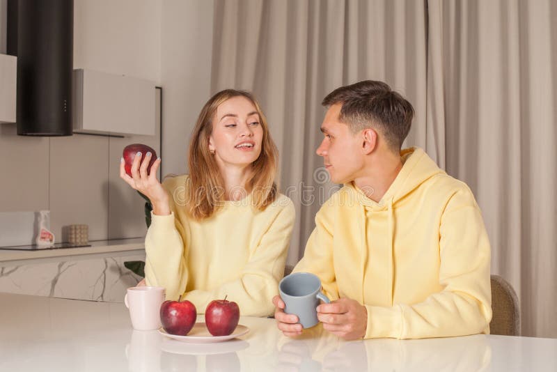 Lovely Couple with Cups, Eating Red Apples and Sitting by the Table ...
